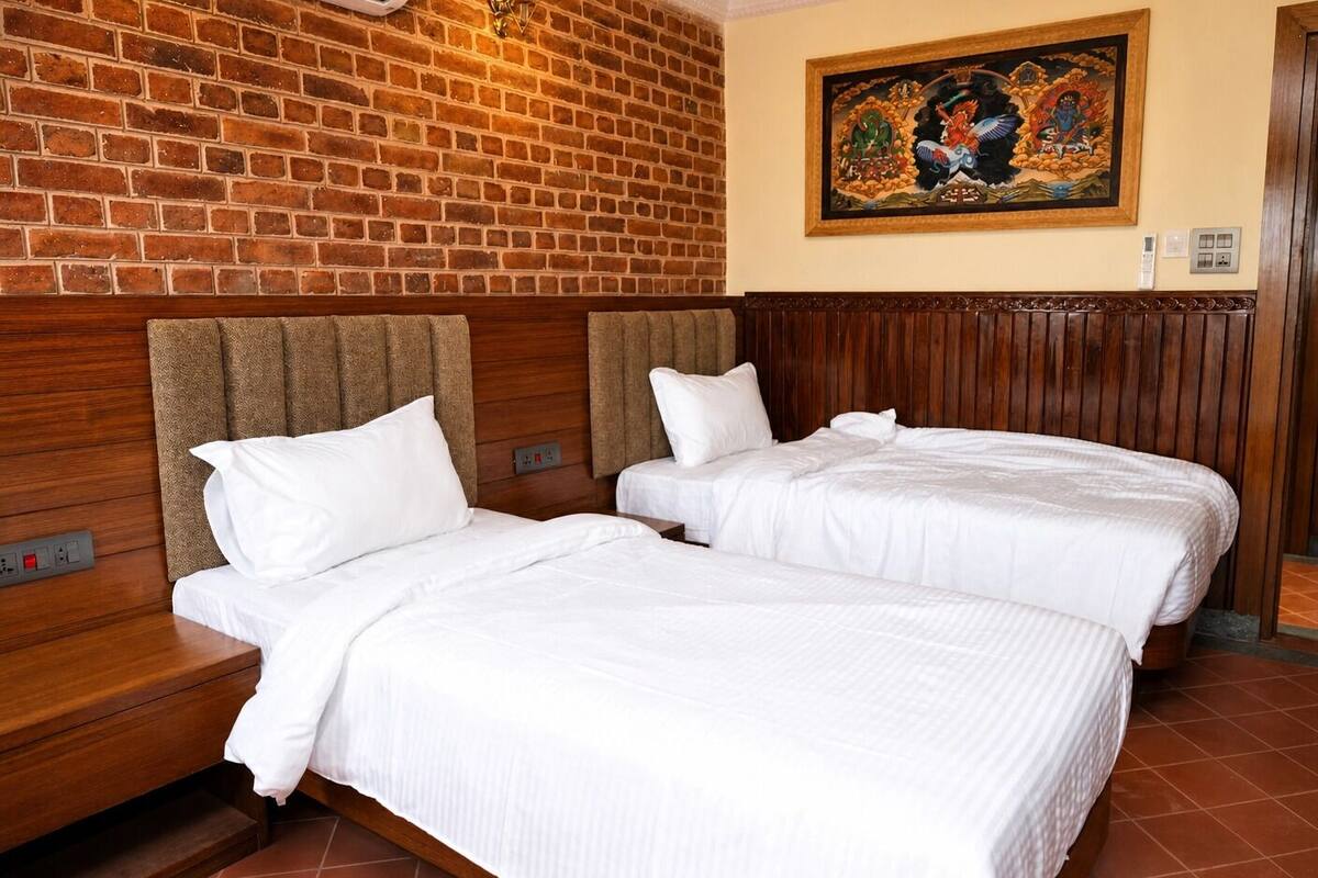 Quarto de hotel com duas camas, parede de tijolos, cabeceira de madeira, um quadro e um termostato.
