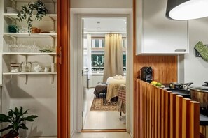 Cozinha moderna com detalhes em madeira, área de jantar com mesa e cadeiras, e vista para um quarto com cama e cortinas.