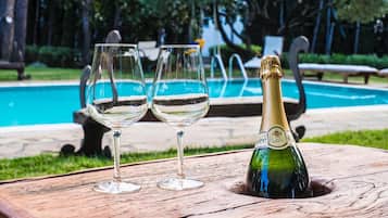 Uma mesa de madeira com dois copos de vinho vazios e uma garrafa de champanhe em frente a uma piscina.