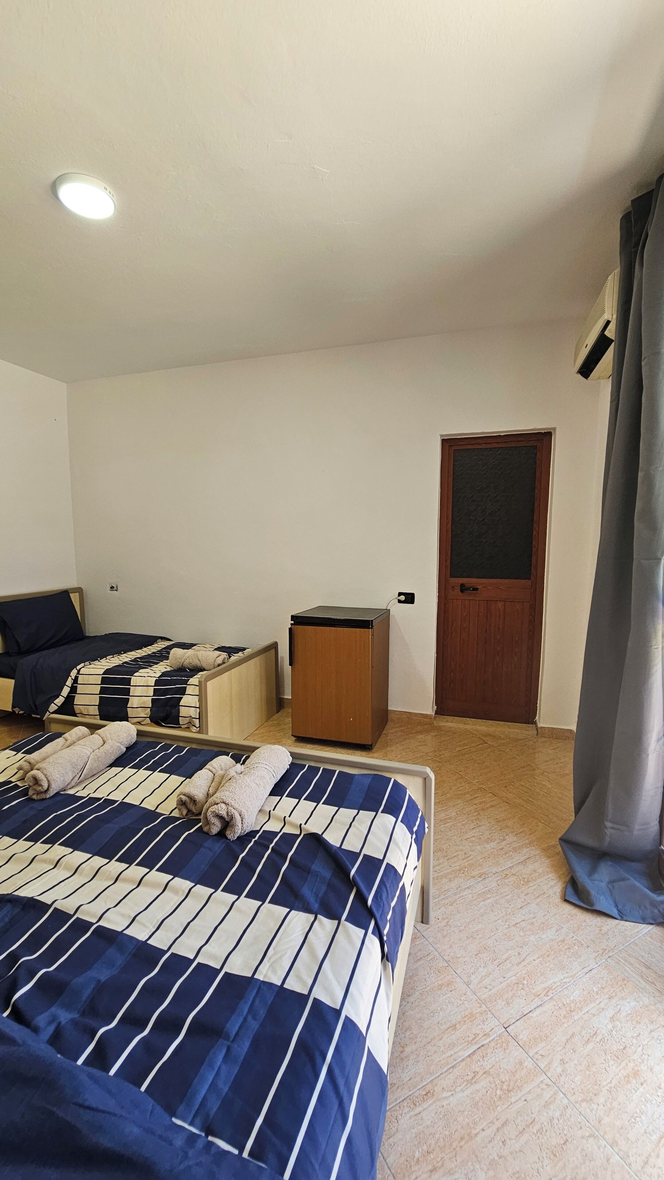 Quarto de hotel com cama, um pequeno armário de madeira, uma porta e uma lâmpada no teto.