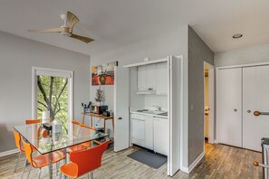 Uma cozinha moderna com armários brancos, uma mesa de jantar de vidro e cadeiras laranja.