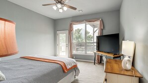 Quarto com cama, ventoinha no teto, televisão e escrivaninha com abajur.
