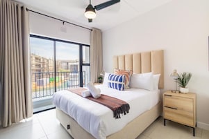 Quarto moderno com uma cama grande, mesa de cabeceira, ventilador de teto e vista para o exterior.