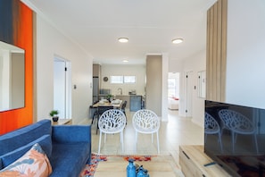Uma sala de estar moderna com um sofá, uma TV de tela plana e um espaço de jantar com cadeiras e uma mesa.