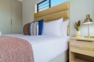 Quarto de hotel com cama, mesa de cabeceira com abajur, janela e armário.