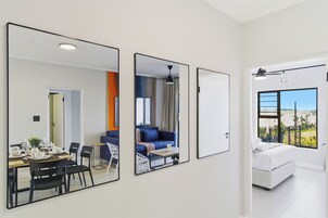 Quarto de hotel moderno com área de jantar, espaço de estar com sofá e mesa de centro, e uma janela grande com vista.