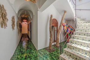 Um corredor com piso de azulejos verdes, escada com degraus estampados e arte decorativa nas paredes.