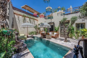 Área de piscina com uma estátua, mobiliário externo e um edifício com detalhes decorativos.