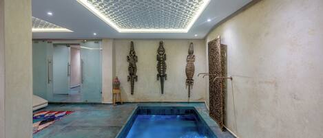 Piscina interior moderna com design geométrico no teto, vista clara da piscina e decoração de parede estampada.