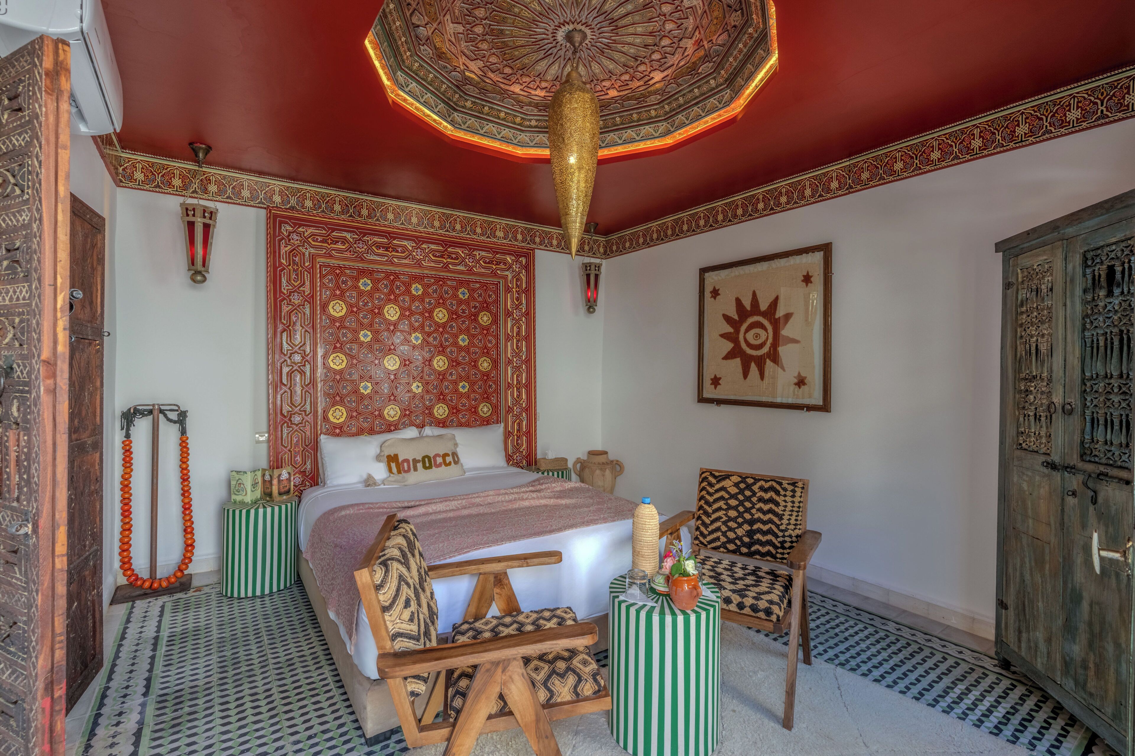 Um quarto tradicional marroquino com cama estampada, uma cadeira de madeira, um armário e teto decorativo.