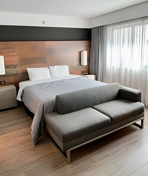 Quarto de hotel moderno com uma cama, um sofá, uma mesa de cabeceira e uma janela com cortinas.