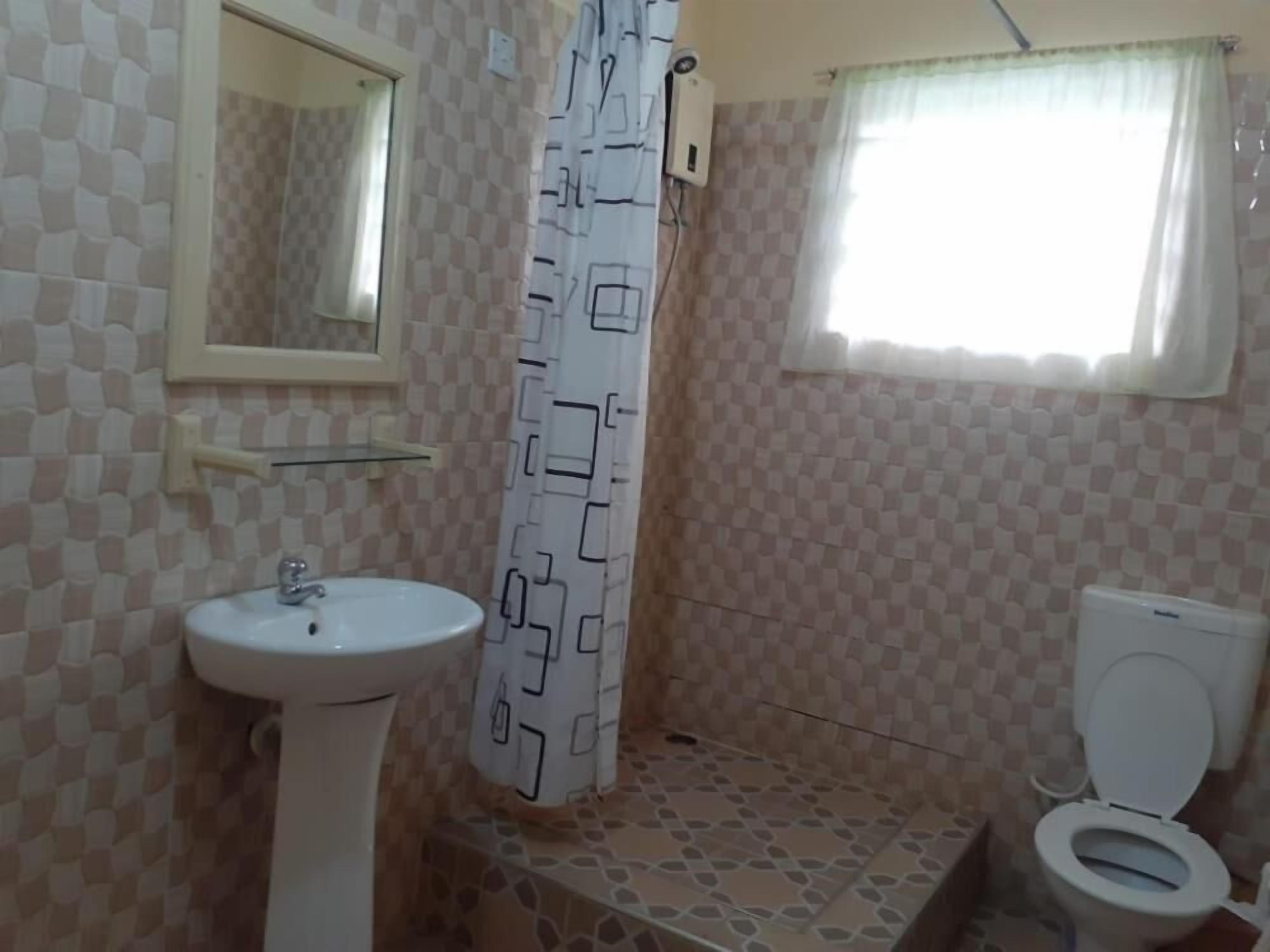 Casa de banho com lavatório, sanita, cortina de chuveiro e janela com cortinas.