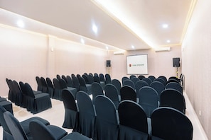 Uma sala de conferências com fileiras de cadeiras, uma tela de projetor e alto-falantes.