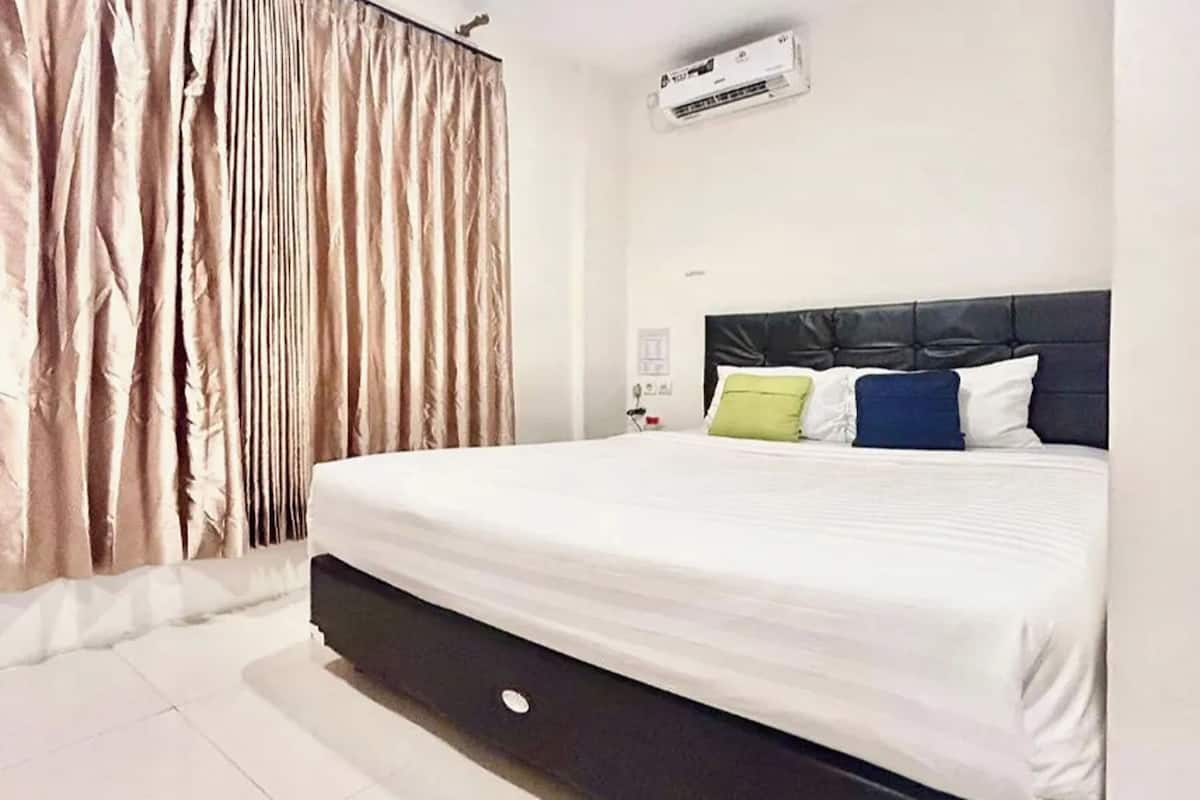 Quarto de hotel com cama, cortinas, ar condicionado e mesa de cabeceira.