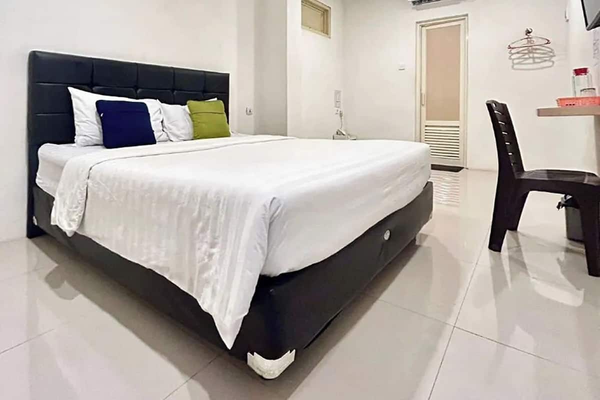 Cama com cabeceira escura, roupa de cama branca e várias almofadas.