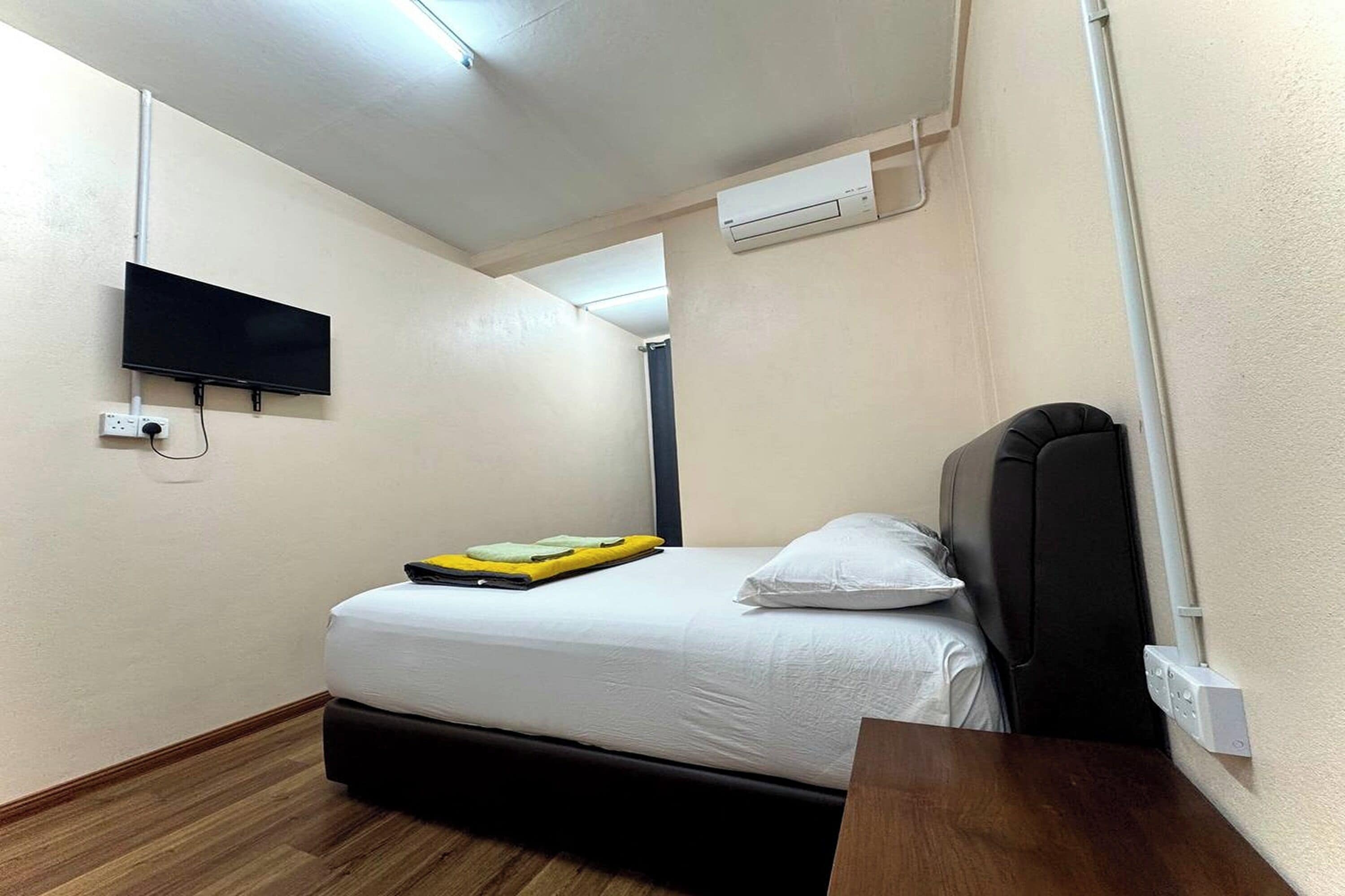 Quarto de hotel com cama, televisão na parede, ar condicionado e piso de madeira.