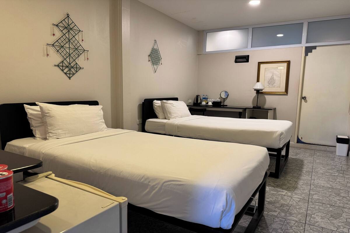 Quarto de hotel com duas camas, uma escrivaninha, uma cadeira, uma mesinha, um abajur e um quadro na parede.