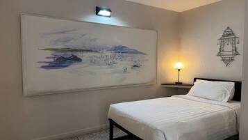 Um quarto com uma cama, uma mesinha de cabeceira, uma luminária na parede e um quadro grande com uma paisagem.
