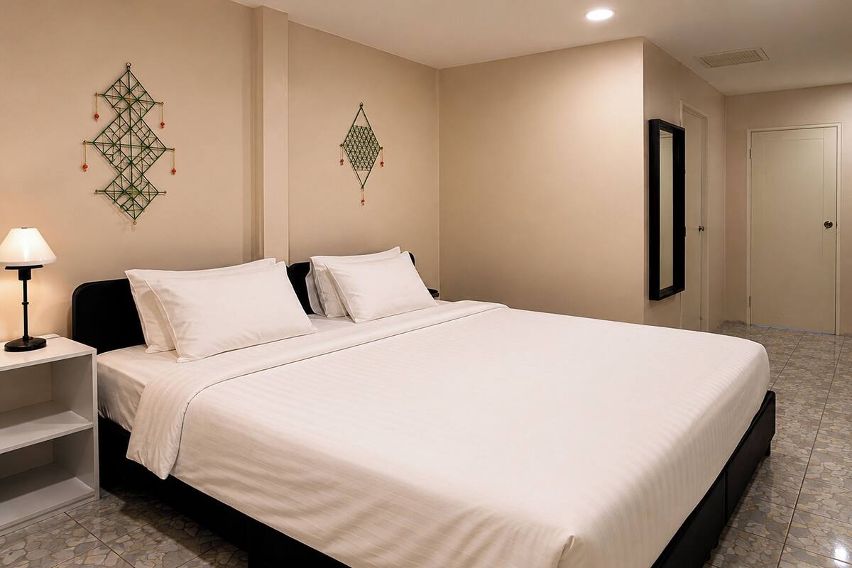 Cama bem arrumada com lençóis brancos, mesa de cabeceira com abajur e detalhes decorativos nas paredes.