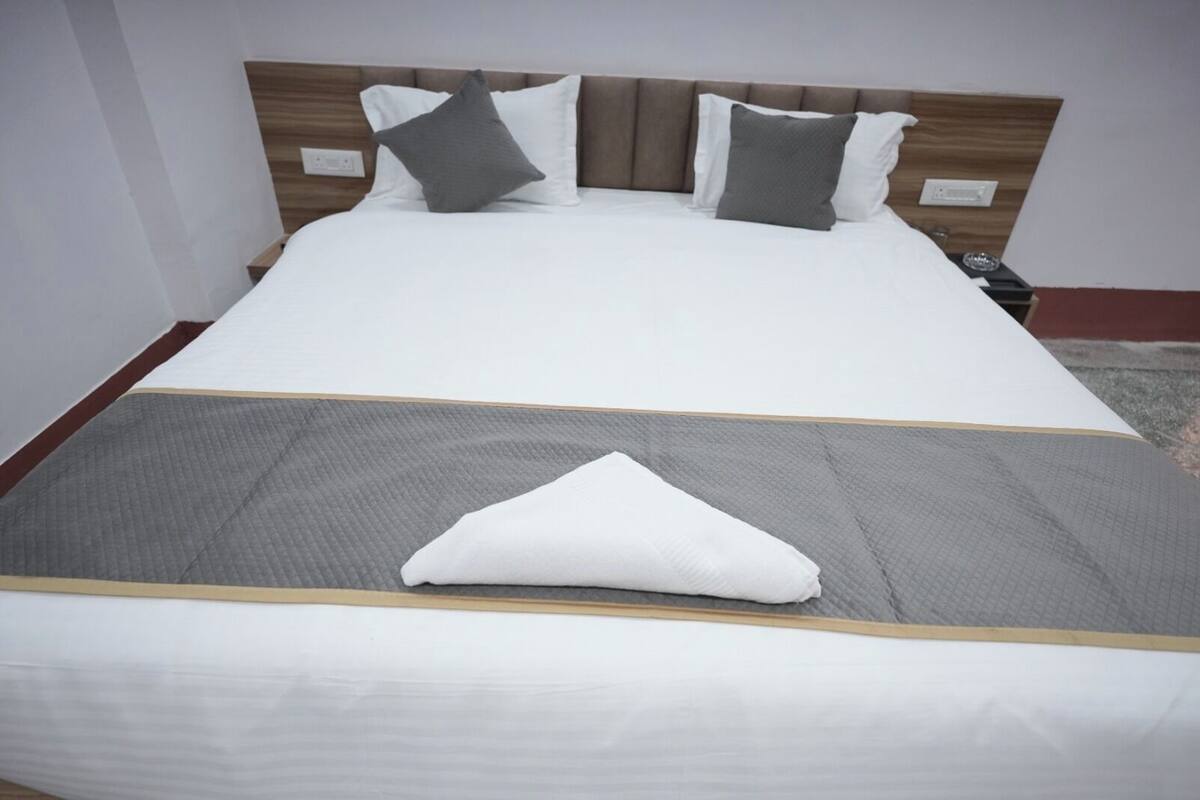 Cama com colcha cinza, almofadas brancas e cabeceira de madeira.