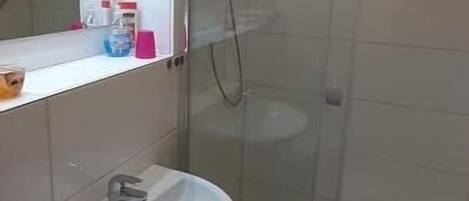 Um banheiro com box de vidro, pia branca e espelho.