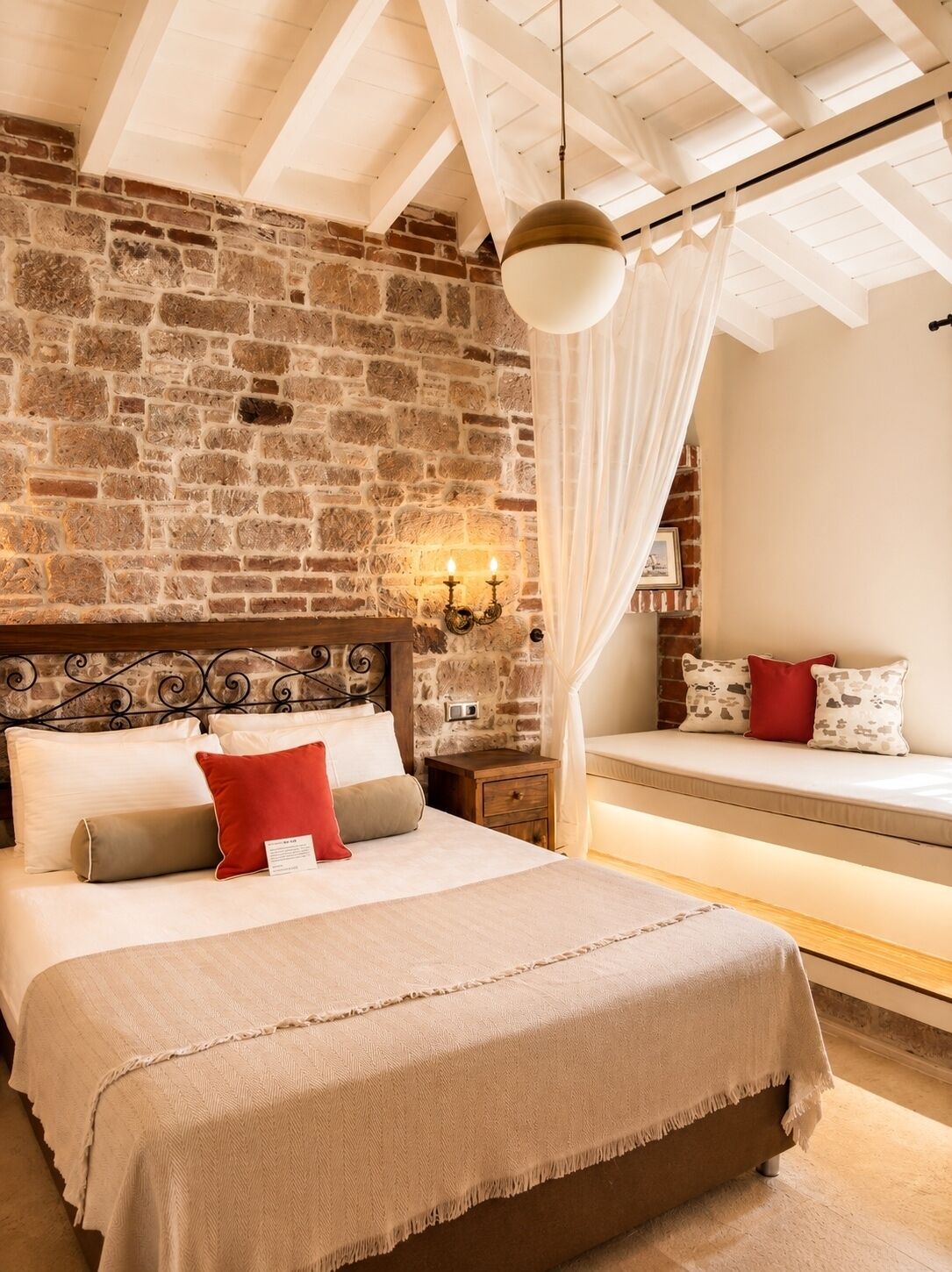 Quarto com parede de pedra, cama com cabeceira, mesas de cabeceira e um assento de janela com almofadas.
