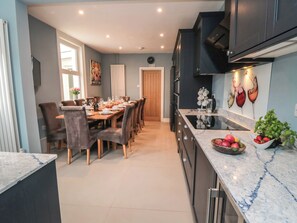 Uma cozinha moderna com armários escuros, bancada de mármore e um espaço de jantar com mesa e cadeiras de madeira.