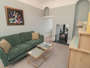Uma sala de estar com um sofá verde, uma mesa de centro de vidro, uma lareira e um quadro na parede.