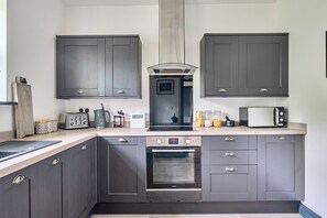 Uma cozinha moderna com armários escuros, forno embutido, micro-ondas e cafeteira.
