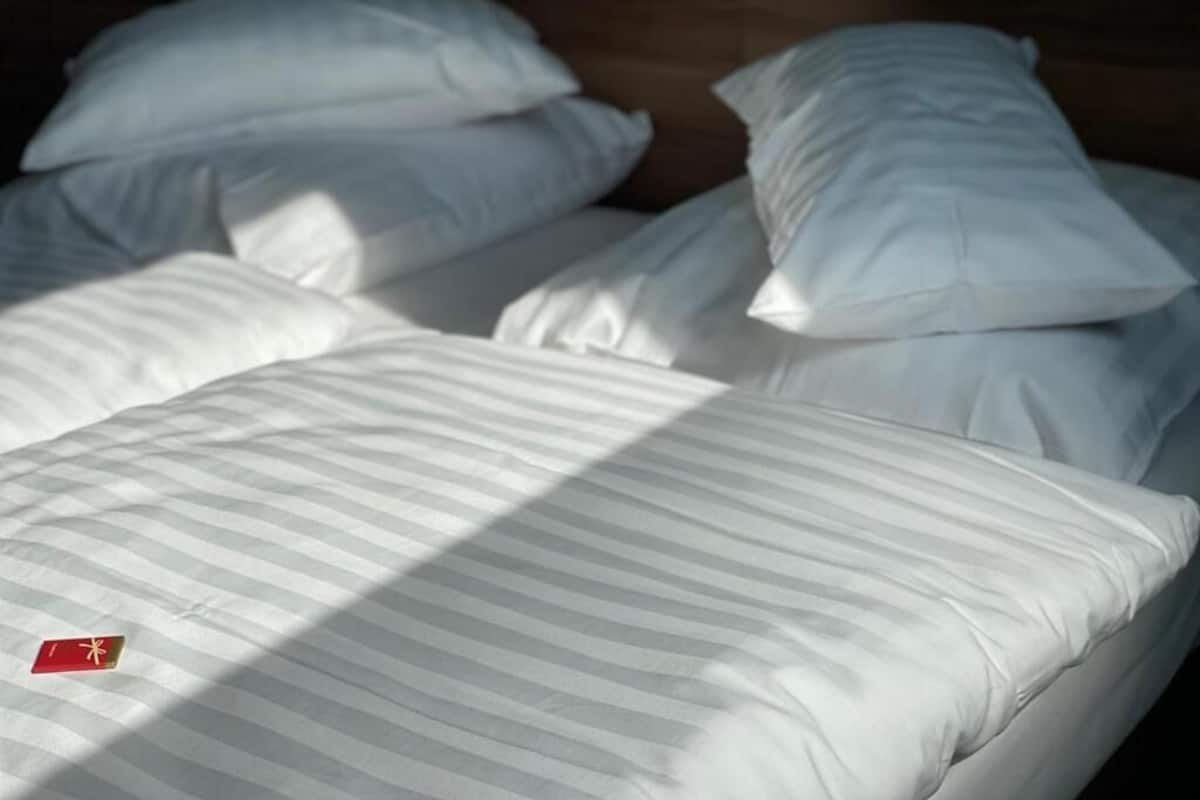Cama com roupa de cama branca e uma pequena bandeira no travesseiro.