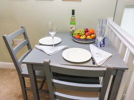 Mesa de jantar posta com pratos, uma tigela de frutas, copos de vinho e uma garrafa de vinho.