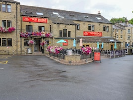 Um edifício com a placa 'Old Bridge Inn & Coffee House', área de estar ao ar livre com guarda-sóis e cestos de flores.