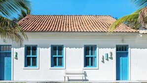 Um edifício branco com portas e janelas azuis, telhado em azulejos e um banco branco na frente.