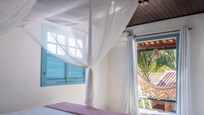 Um quarto com uma cama, uma janela com persianas azuis e vista para um telhado cerâmico.