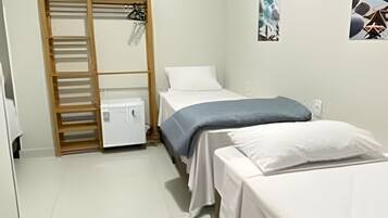 Quarto pequeno e limpo, com duas camas, um guarda-roupa de madeira e uma mesa.