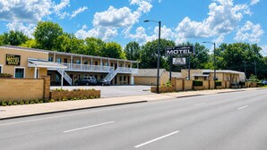 Um motel com placa, estacionamento e céu limpo.