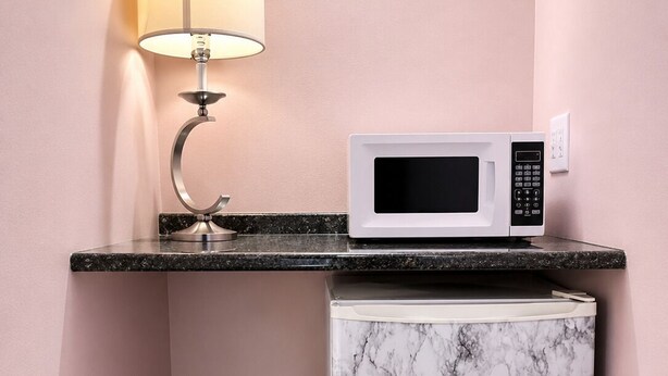 Uma cozinha compacta equipada com micro-ondas, mini-geladeira com padrão marmorizado e luminária de parede.