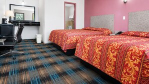 Quarto de hotel com duas camas, uma escrivaninha, uma cadeira, um espelho e uma porta.