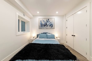 Um quarto com cama, janela, quadro, mesas de cabeceira e guarda-roupa.