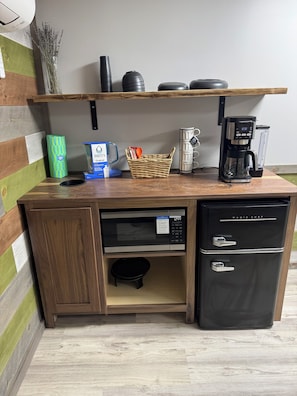 Uma cozinha compacta equipada com micro-ondas, máquina de café e mini-geladeira.