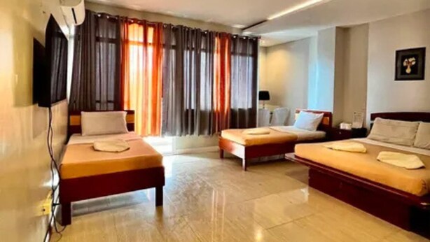 Quarto de hotel com uma cama grande, duas camas menores, televisão de tela plana e uma janela ampla com cortinas.