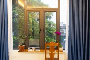 Uma janela com vista para vegetação, uma cadeira de madeira e um vaso com planta.