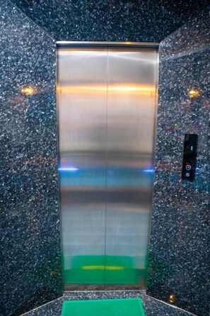 Um elevador com interior metálico e um tapete verde na base.