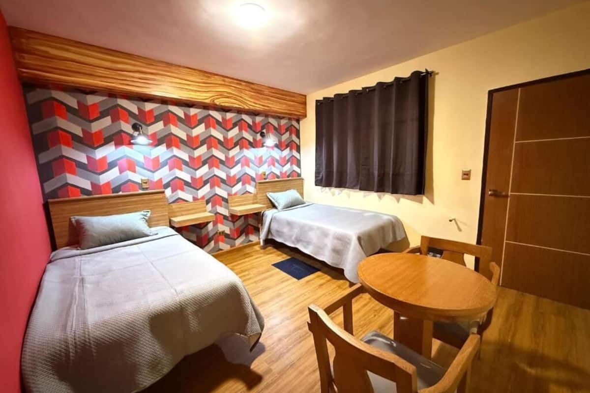 Quarto com duas camas, uma mesa de madeira e uma cadeira.