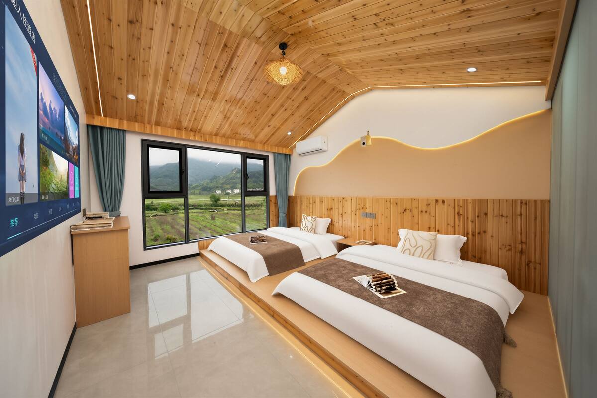 Quarto com duas camas, teto de madeira, uma janela ampla com vista e televisão fixada na parede.