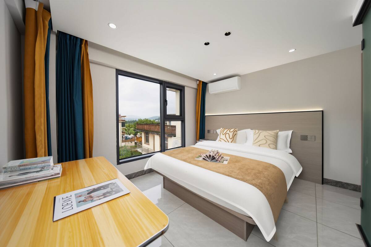 Quarto de hotel moderno com uma cama grande, uma mesa de madeira e uma janela com vista.
