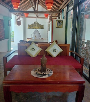 Quarto com mesa de madeira, duas cadeiras, sofá vermelho e uma estátua decorativa de Buda.
