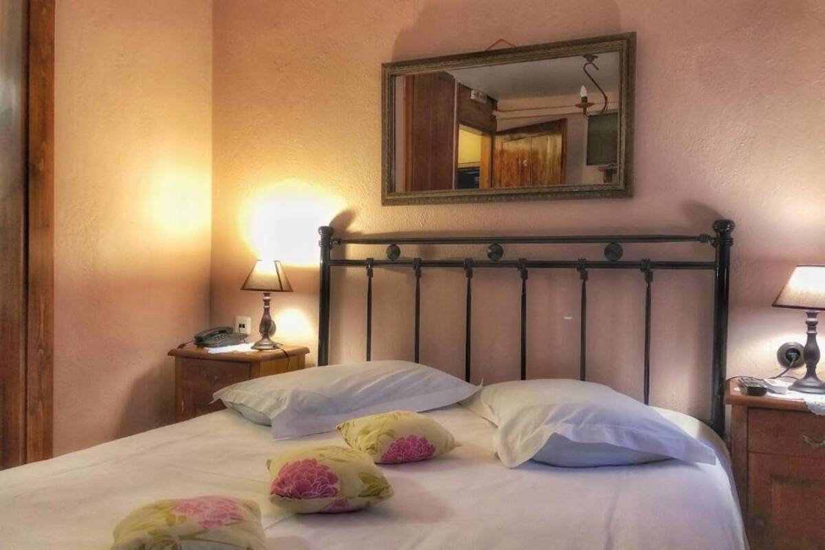 Um quarto com uma cama, duas mesas de cabeceira, um criado-mudo, um espelho e um abajur.