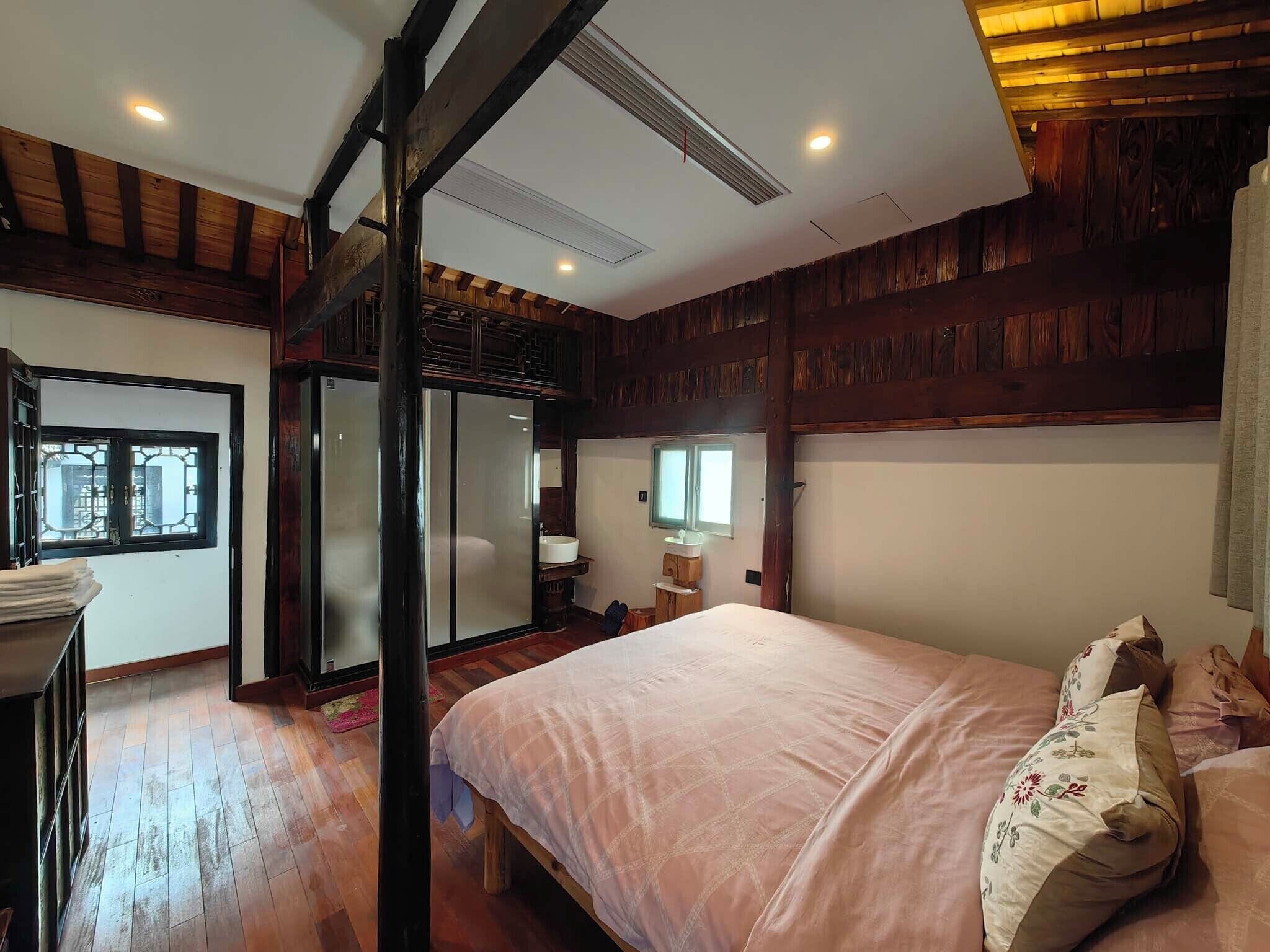 Quarto com cama grande, paredes de madeira, porta deslizante e banheiro pequeno com pia e espelho.