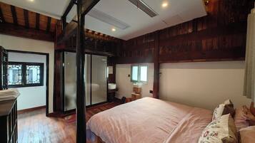 Quarto com cama grande, paredes de madeira, porta deslizante e banheiro pequeno com pia e espelho.